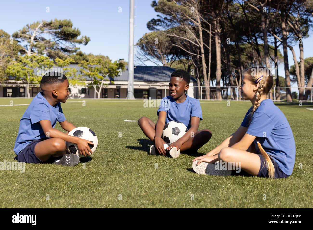 Diverse teenage soccer players wearing blue shirts sitting on soccer ...