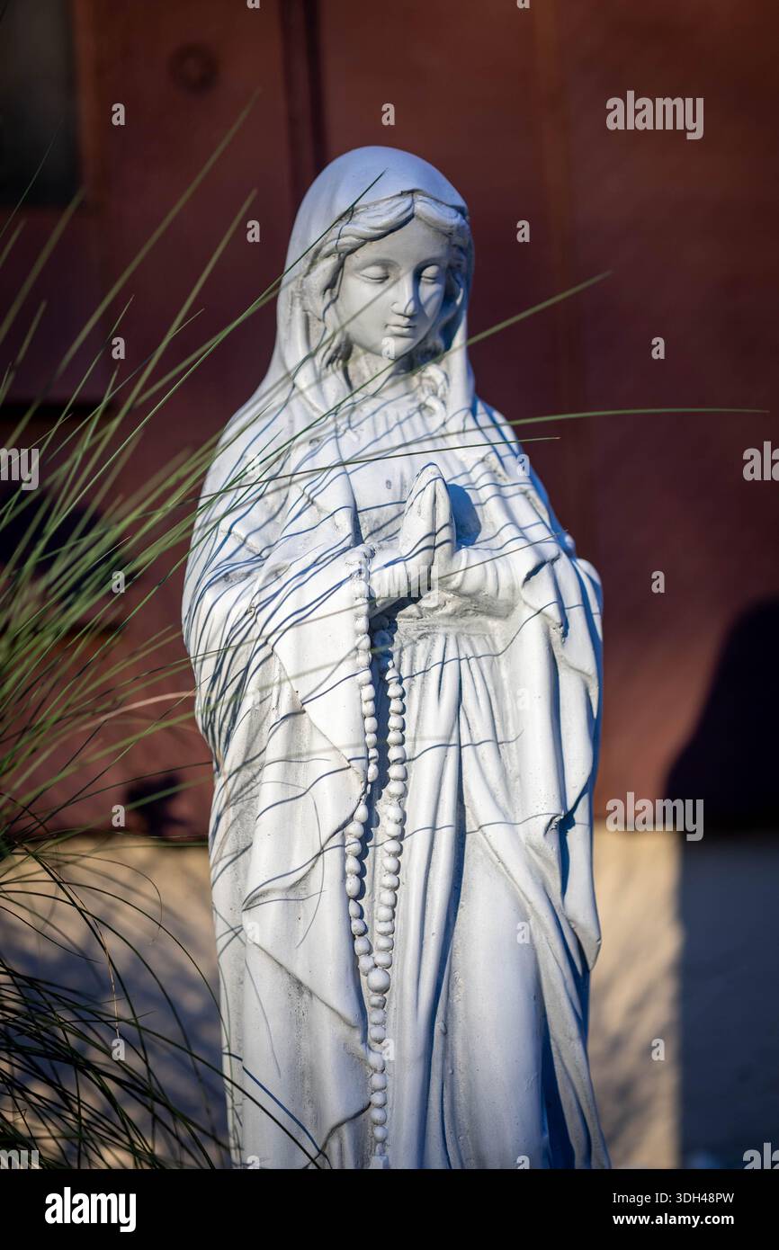 A close-up view of a white concrete garden statue of the Virgin Mary ...