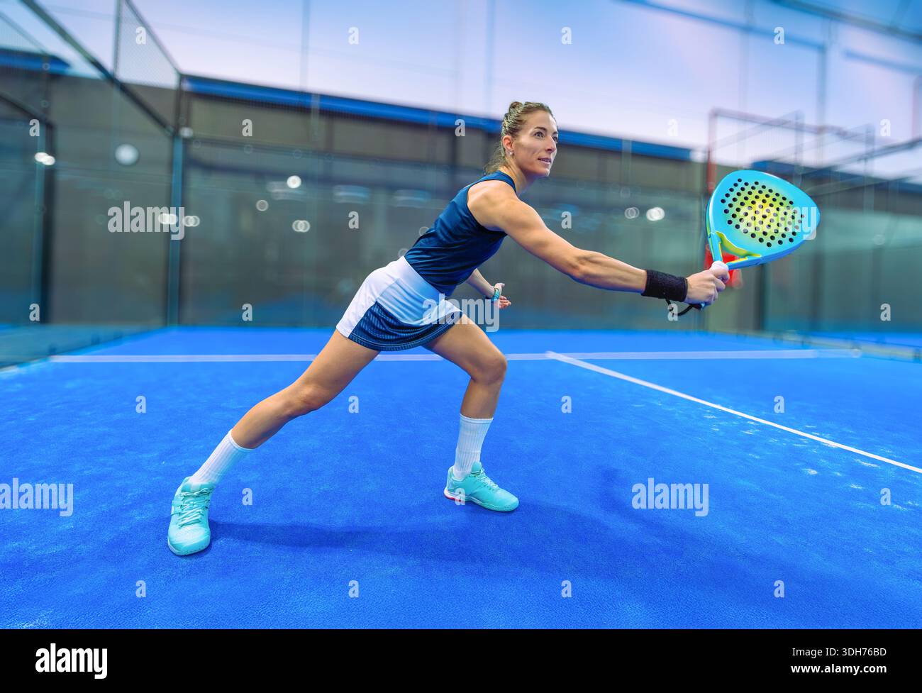 Determined female padel player in action performing a low backhand ...