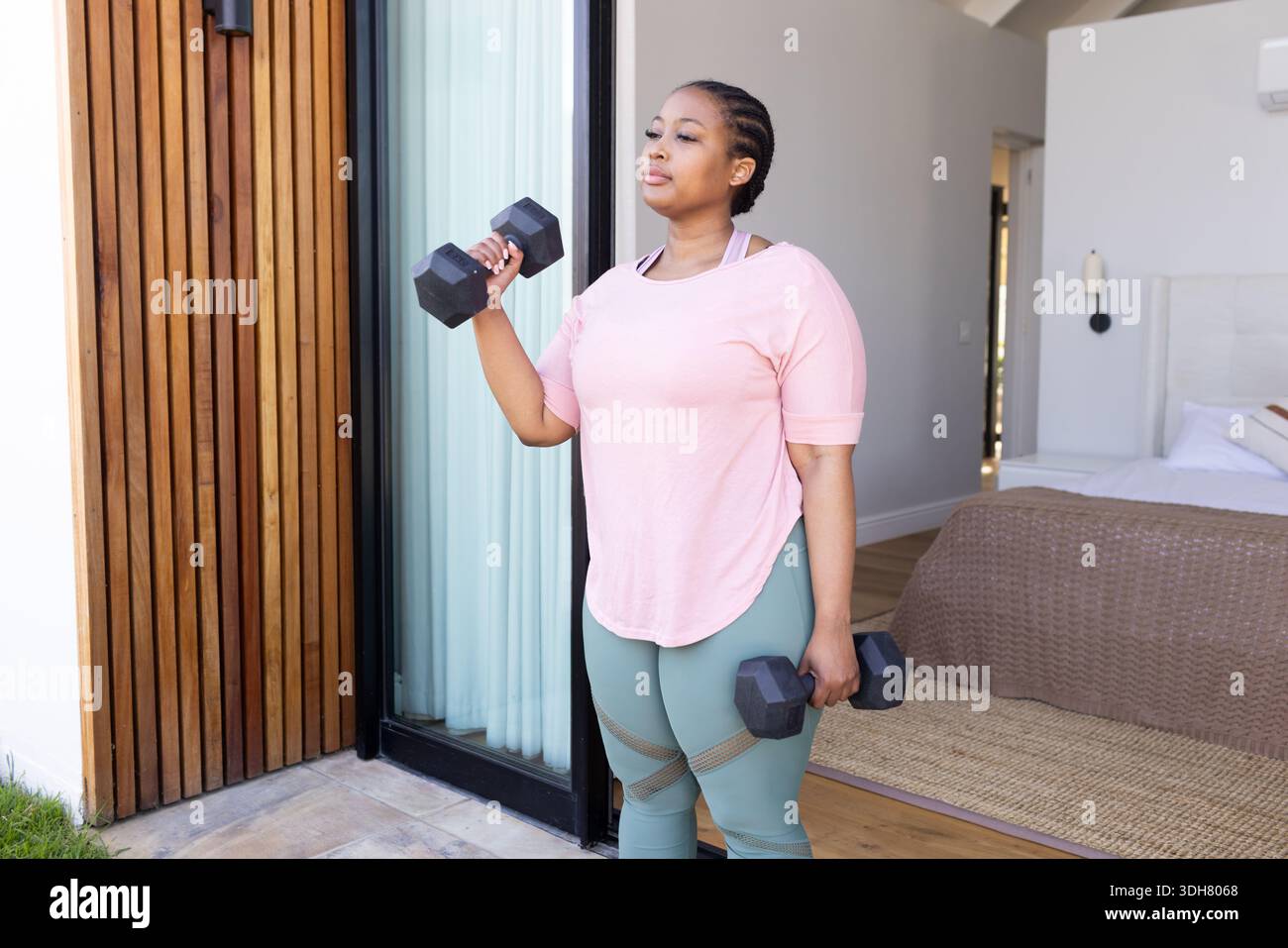 African American woman wearing top and leggings doing biceps curl with ...