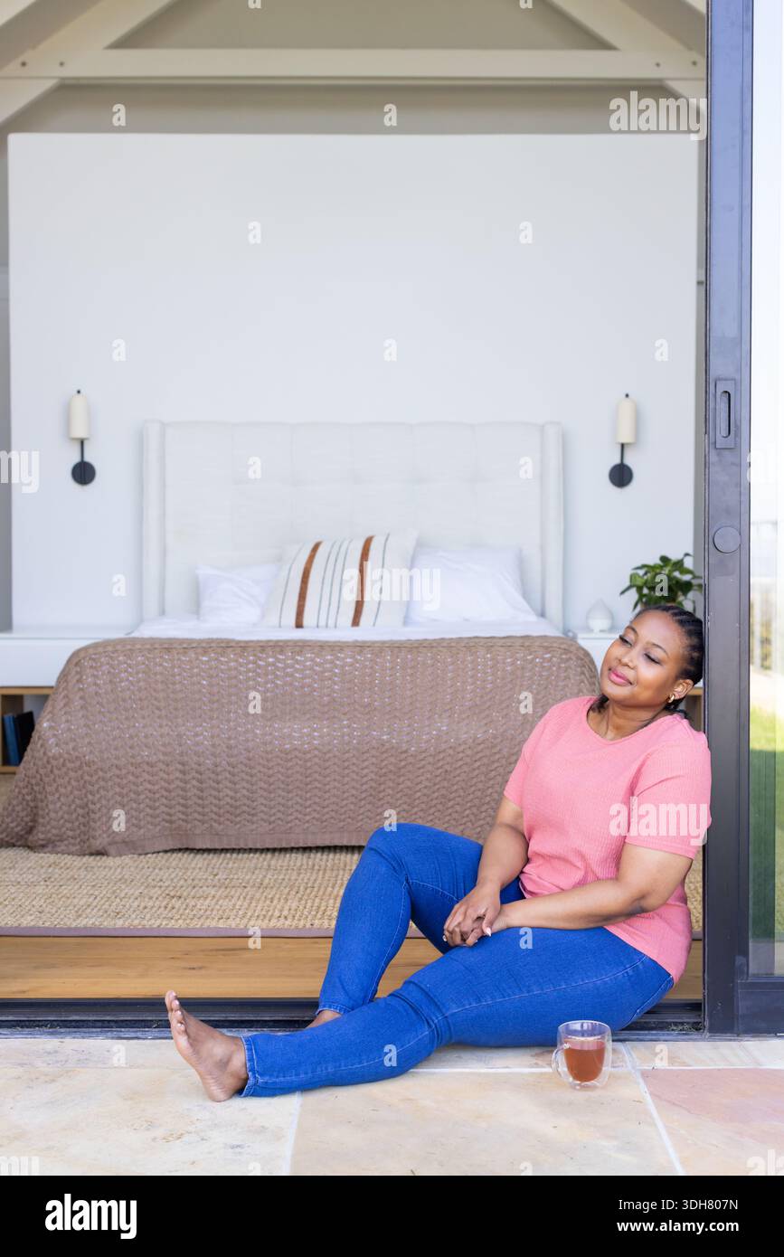 African American woman sitting on threshold of sliding door at bedroom ...