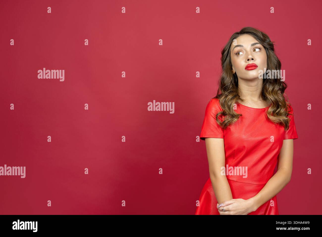 Beautiful brunette woman saddened in a red dress on a red background ...