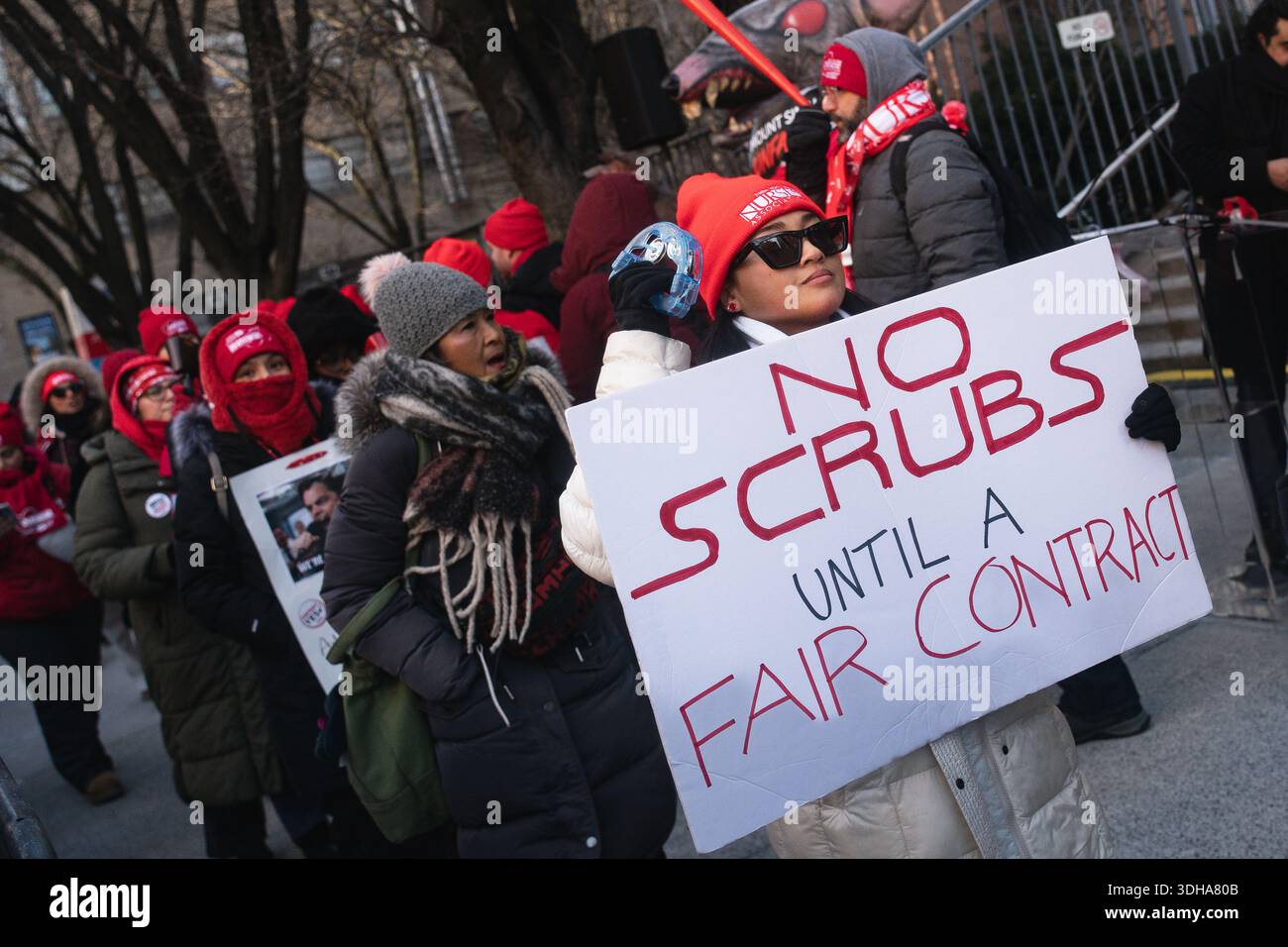 A nurse with a sign that reads "No scrubs until a fair contract ...