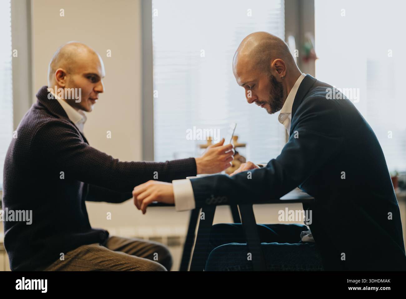 Two clean-cut men in a modern office share a focused moment at a desk ...
