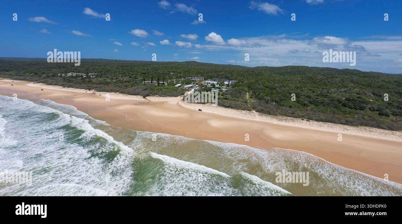 Aerial view of waves crashing onto the sandy beach edged by dense green ...