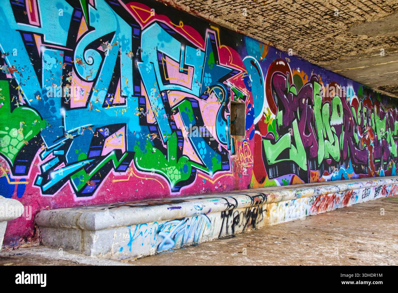 Vibrant graffiti art covers a curved concrete wall with a stone bench ...