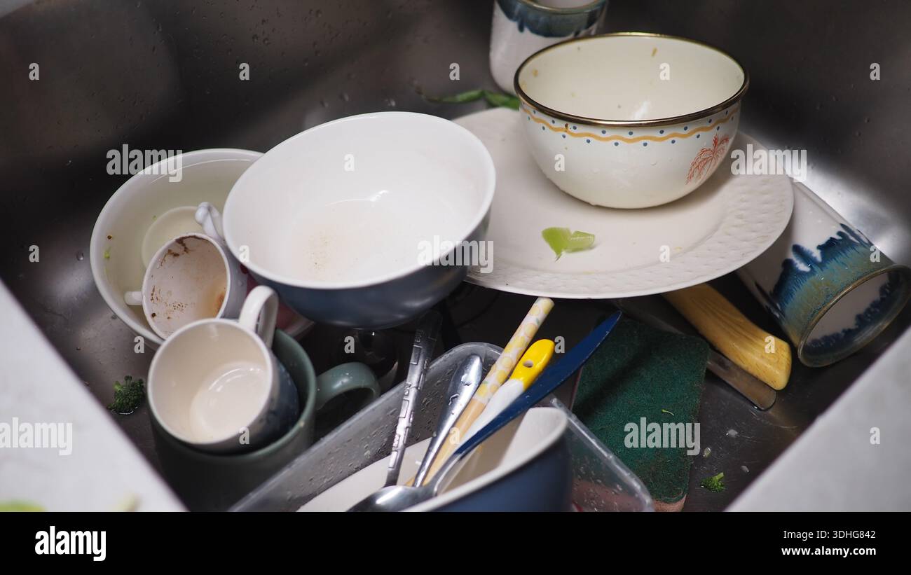 Dirty dishes piled in sink with food remnants and utensils Stock Photo ...
