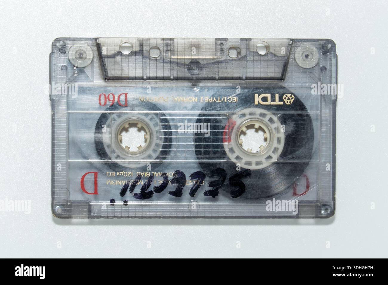 A clear audio cassette rests on a white surface, revealing the magnetic ...