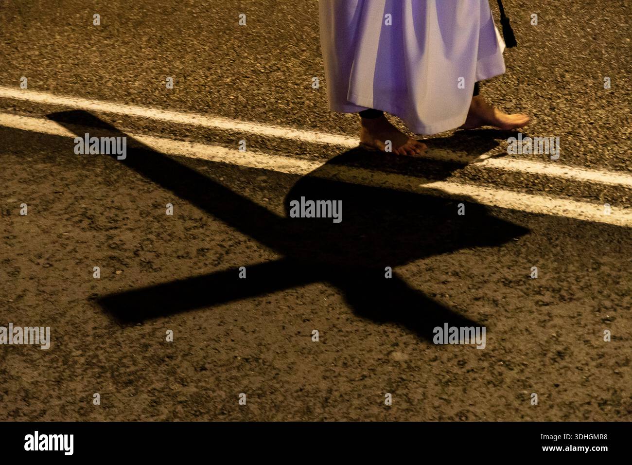 A person walks barefoot on a road at night, casting a shadow shaped ...