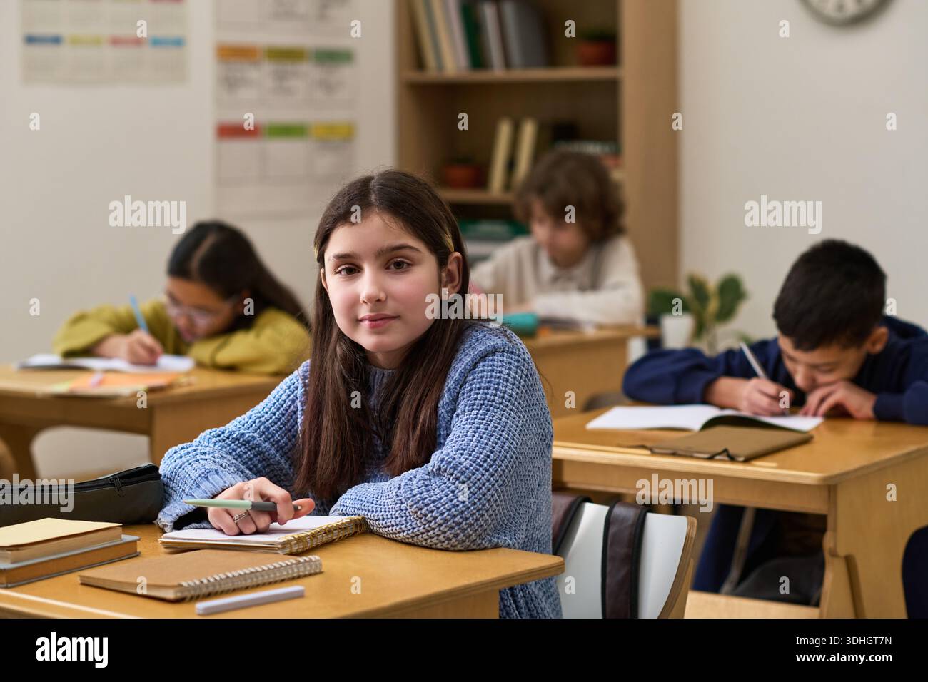 Portrait of Caucasian preteen girl sitting at desk in classroom looking ...