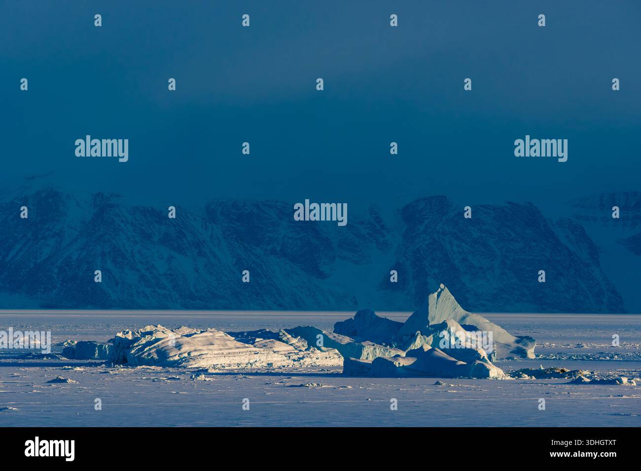 An iceberg is seen floating in the sea in front of the mountains near ...