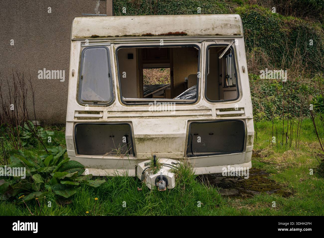 Front view of an abandoned caravan standing on overgrown ground, with ...
