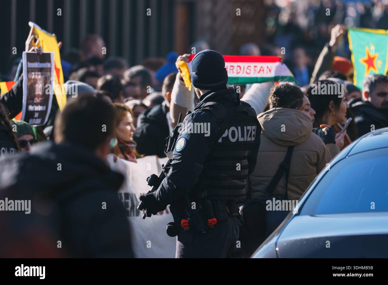 Police officer standing in crowd observing protest with kurdistan flags ...