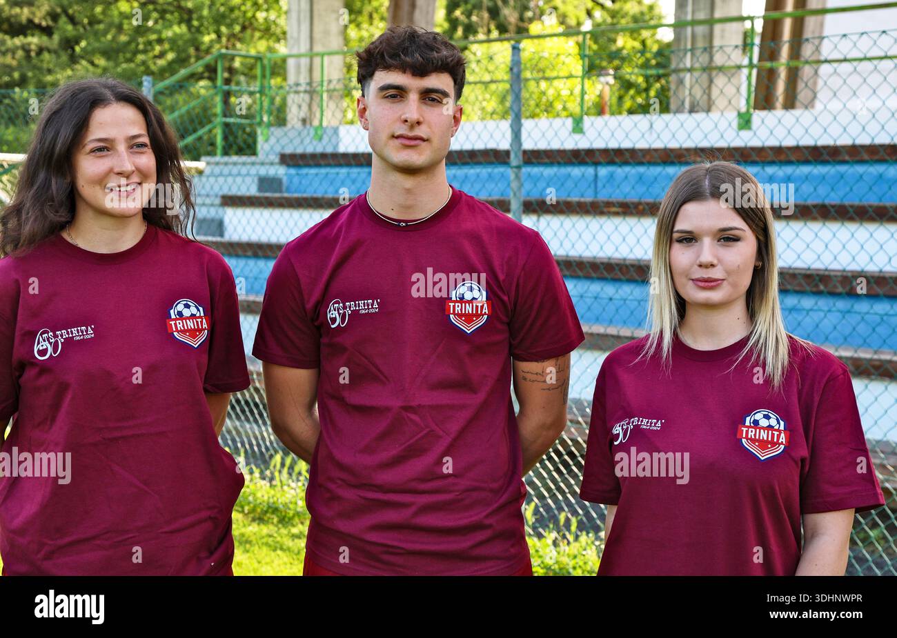 Three young soccer players wearing maroon team jerseys stand together ...