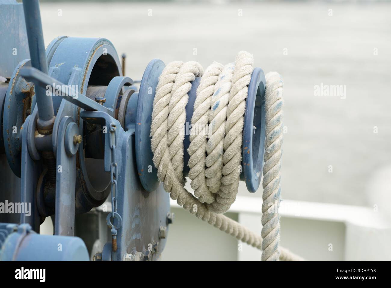 A marine winch with thick coiled rope is mounted on a ship deck ...