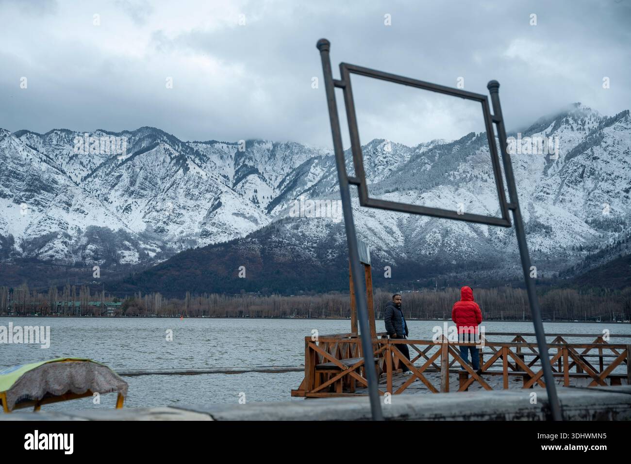 Tourists stand on a jetty on the bank of Dal Lake with snow-covered ...