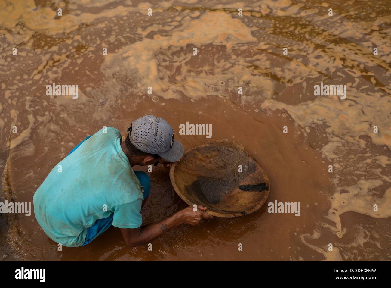A man pans for gold in a pond next to a mill where rock and sediment ...
