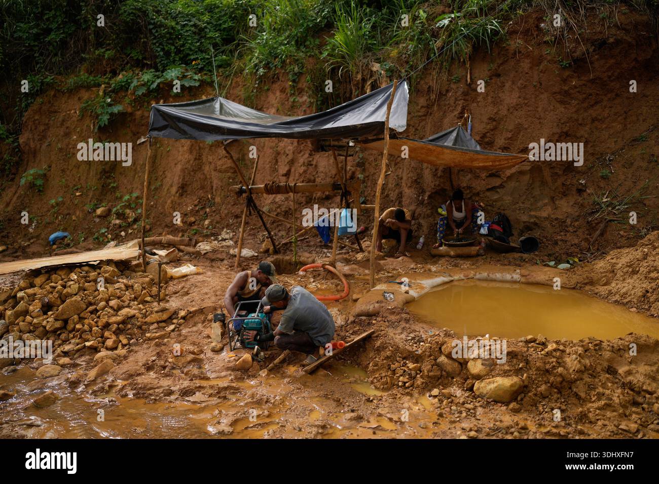A miner sets up a pump to remove water from a pit at a gold mining site ...