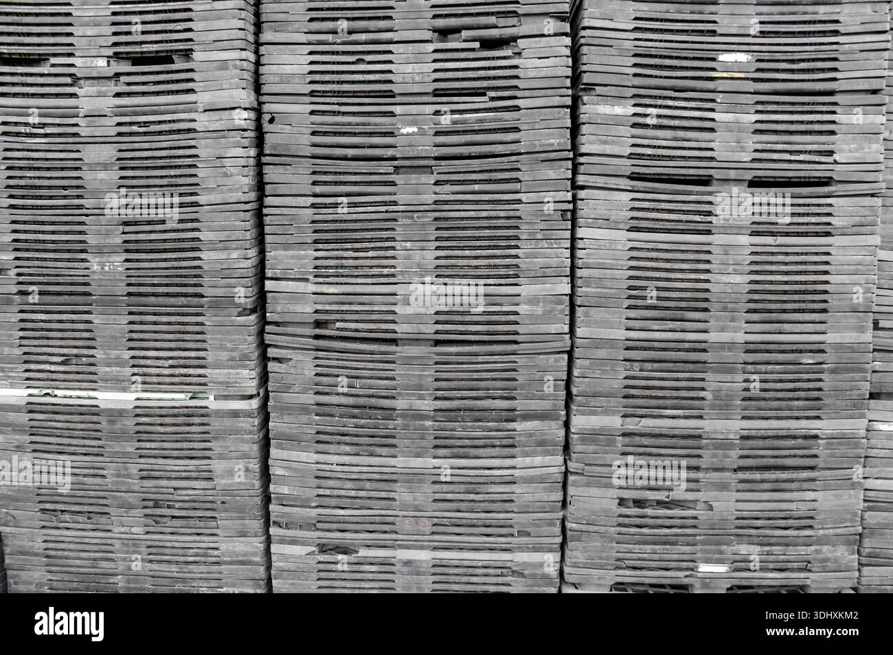 A dense stack of black plastic industrial pallets, featuring a slatted ...
