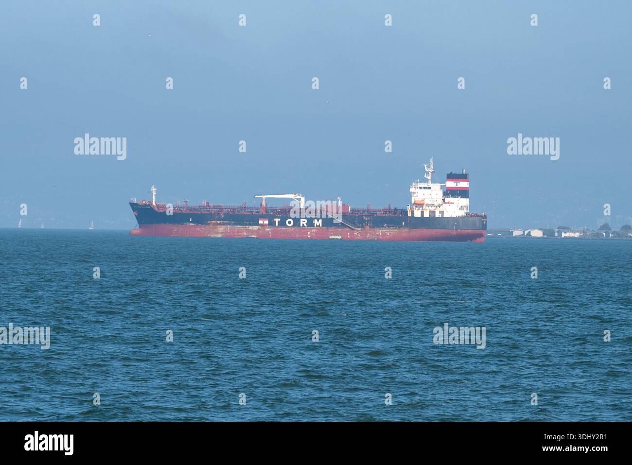 Large cargo ship labeled "TORM" sailing on calm blue water with hazy ...