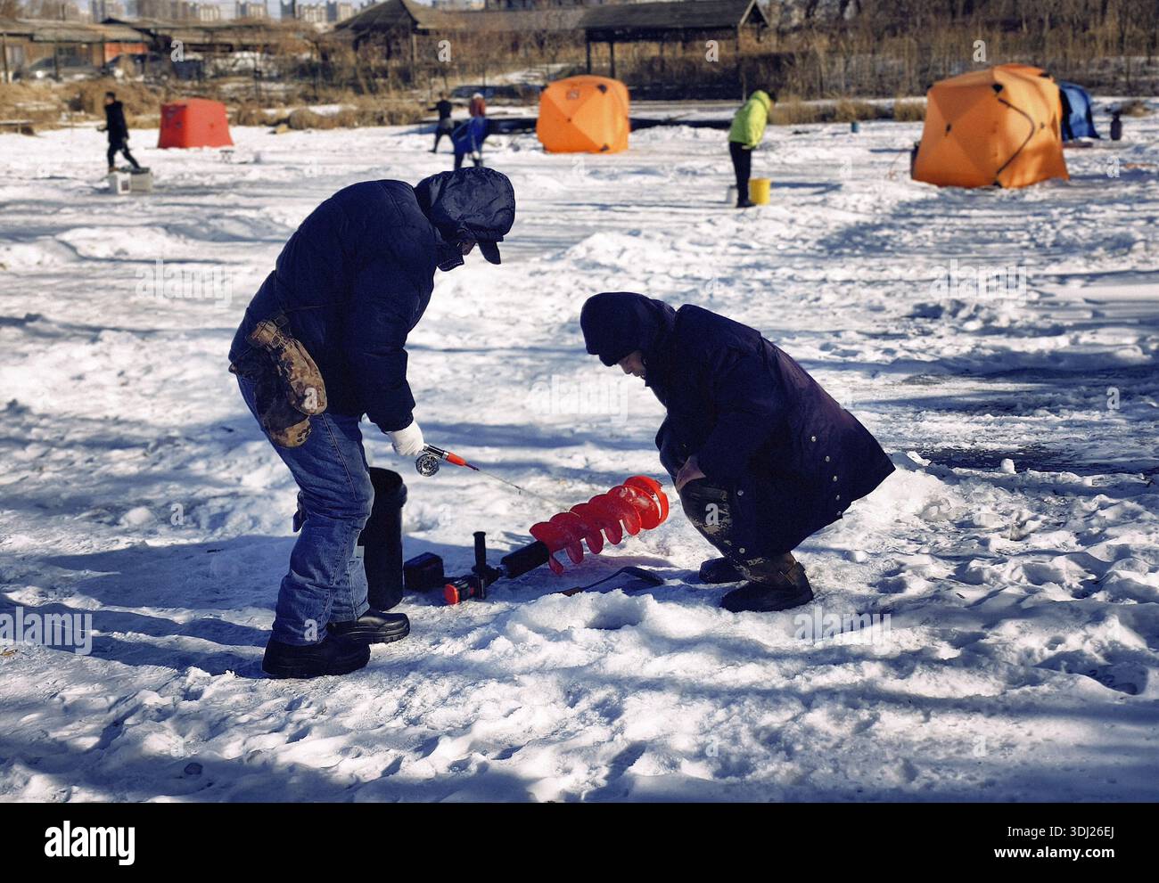 A fishing enthusiast digs a hole on the ice cover of a water space in ...