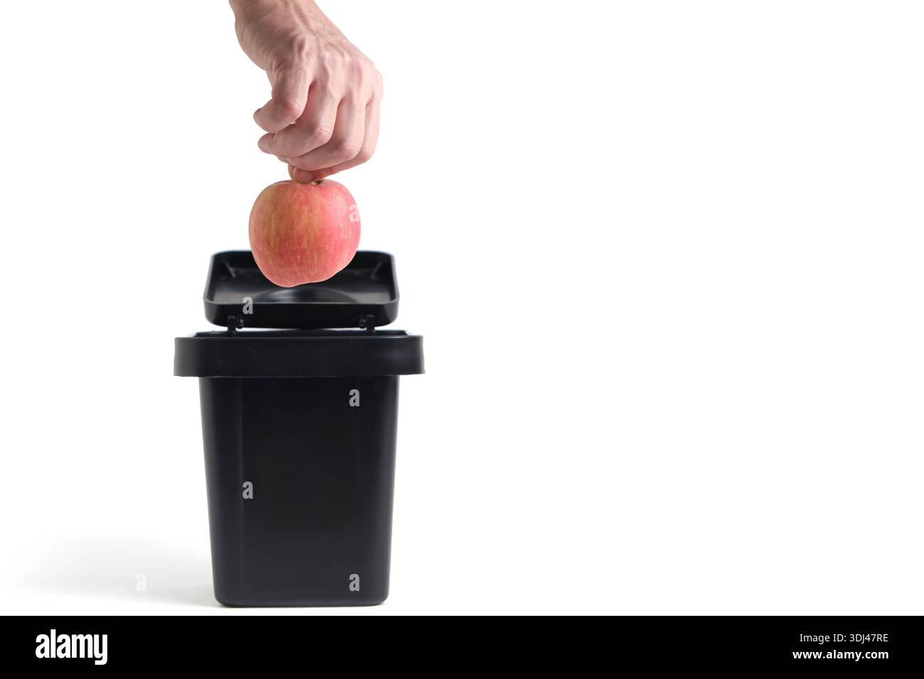 Hand throwing fresh red apple into trash bin, highlighting food waste ...