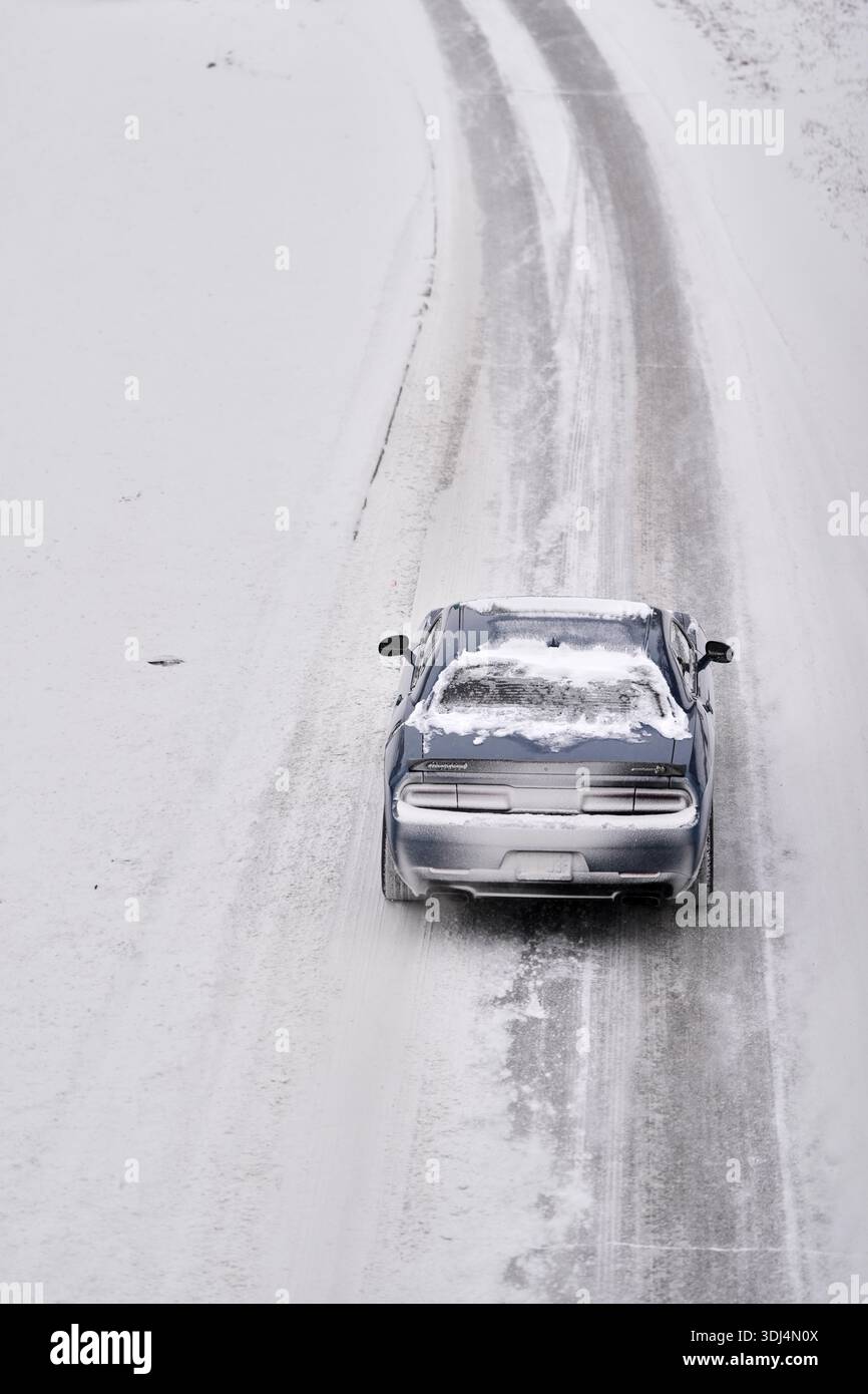 A car travels down a snow-covered road as a winter storm passes through ...