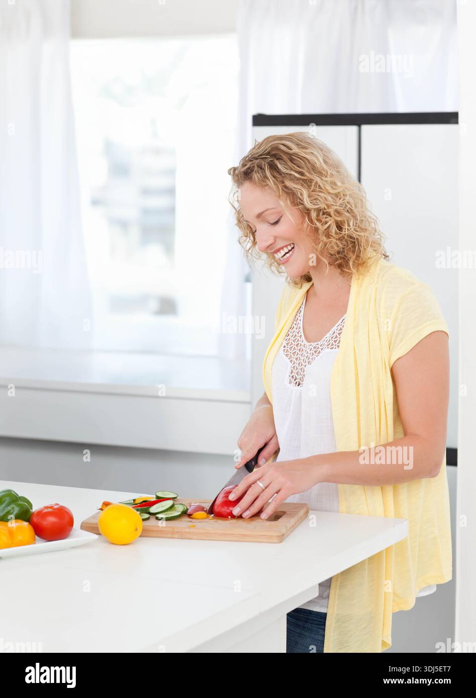 Red bell pepper is being sliced on wooden cutting board at white ...