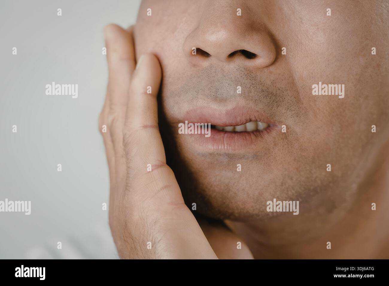 A close-up image of a man holding his jaw with his hand, appearing to ...