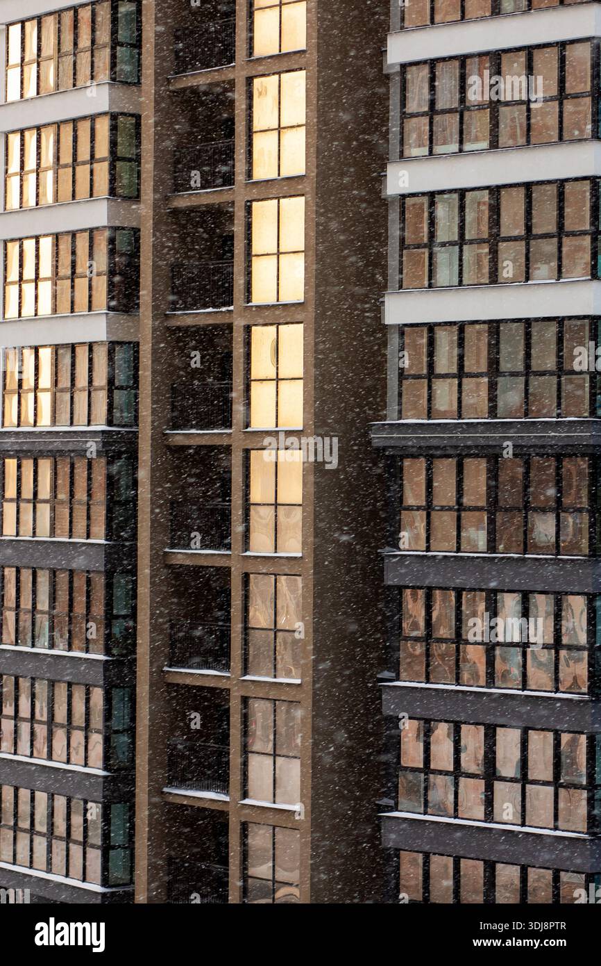 high rise office facade with snow. Vertical grid of glowing windows and ...