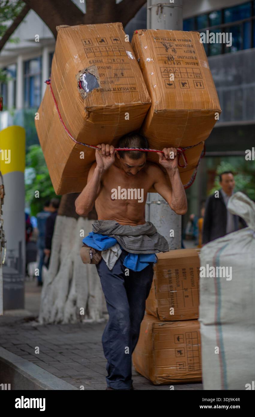 Man carrying two large bundles of clothes on his back, attached to a ...