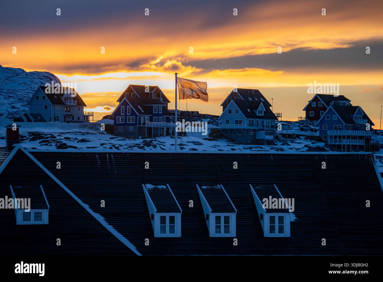 A Greenland flag flies full mast at sunrise over houses in Nuuk ...