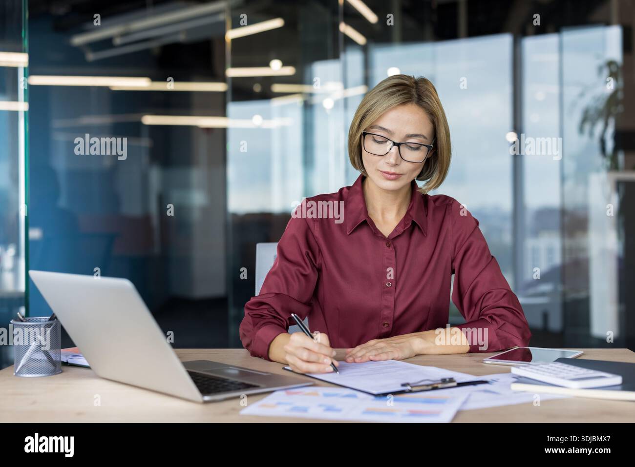 Young businesswoman reviewing financial documents and writing notes at ...
