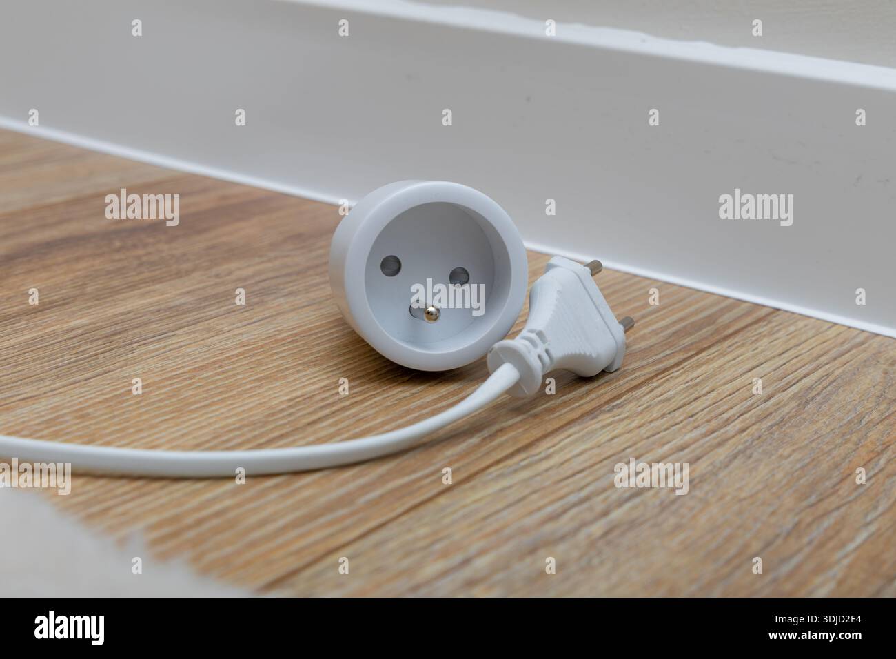 A plug with a cable placed on a wooden floor, a smart electrical outlet ...