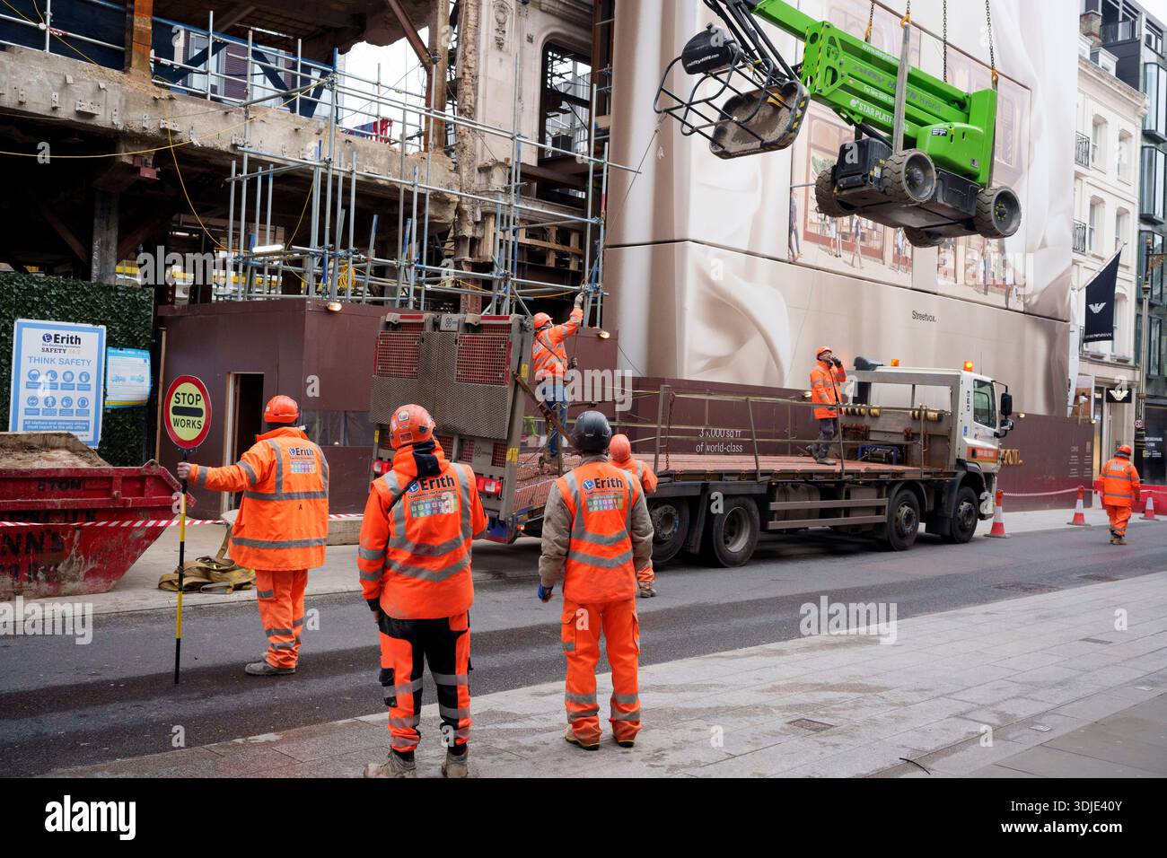 A team of construction workers watch the lowering of an industry ...