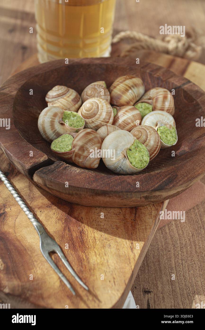 Snails cooked with herb oil on a wooden plate, served with white wine ...