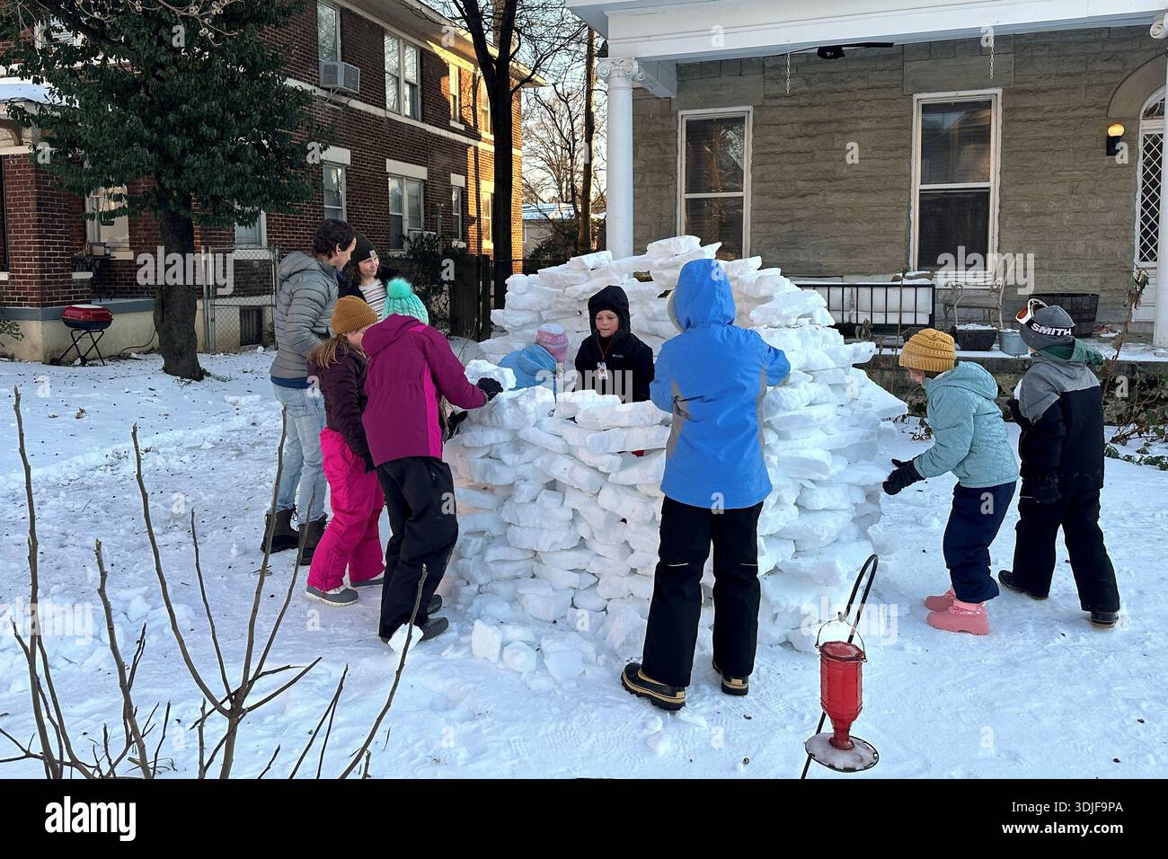 A group of children and adults build an igloo in the front yard of a ...