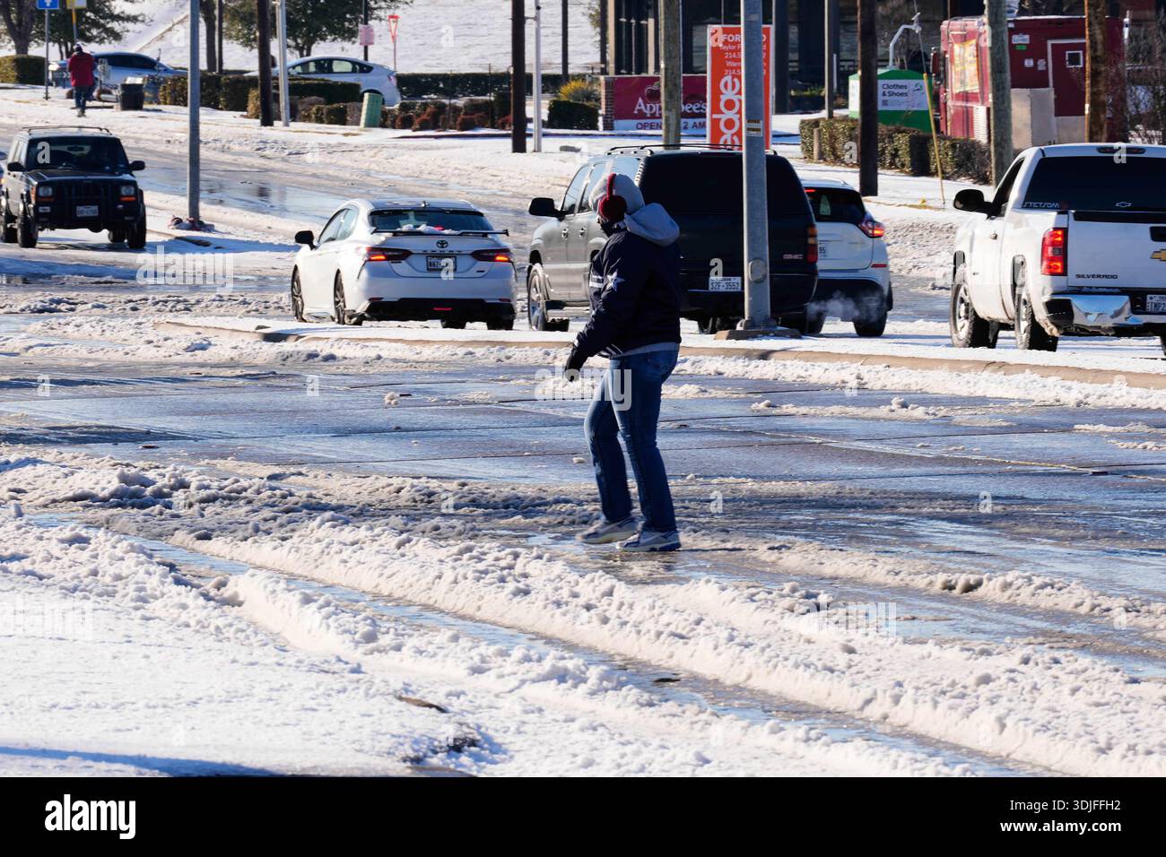 A pedestrian walks through ice and slush as she crosses a major road ...