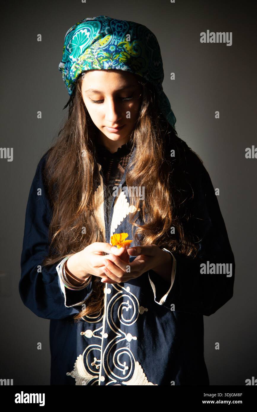 Young woman wearing a patterned headscarf and dark clothing, holding a ...