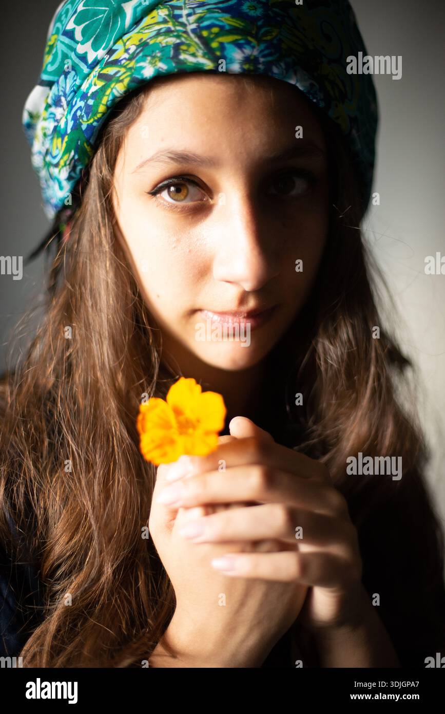 Young woman wearing a patterned headscarf and dark clothing, holding a ...