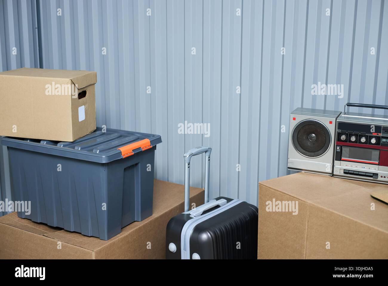 Stacked cardboard boxes, plastic storage container, hard shell suitcase ...