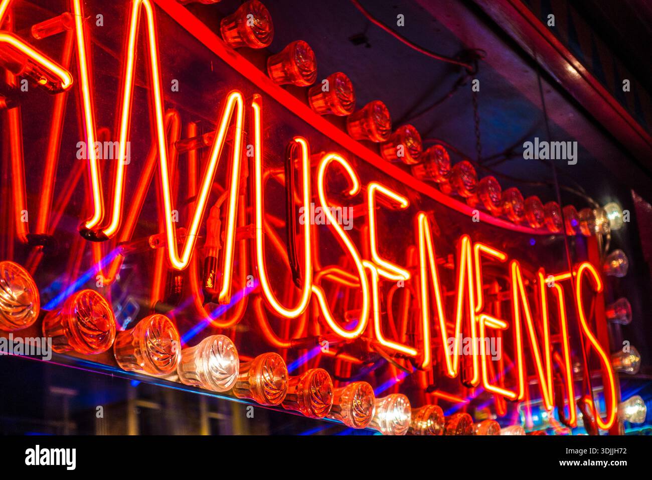Close-up of a glowing red neon "AMUSEMENTS" sign outside a traditional ...