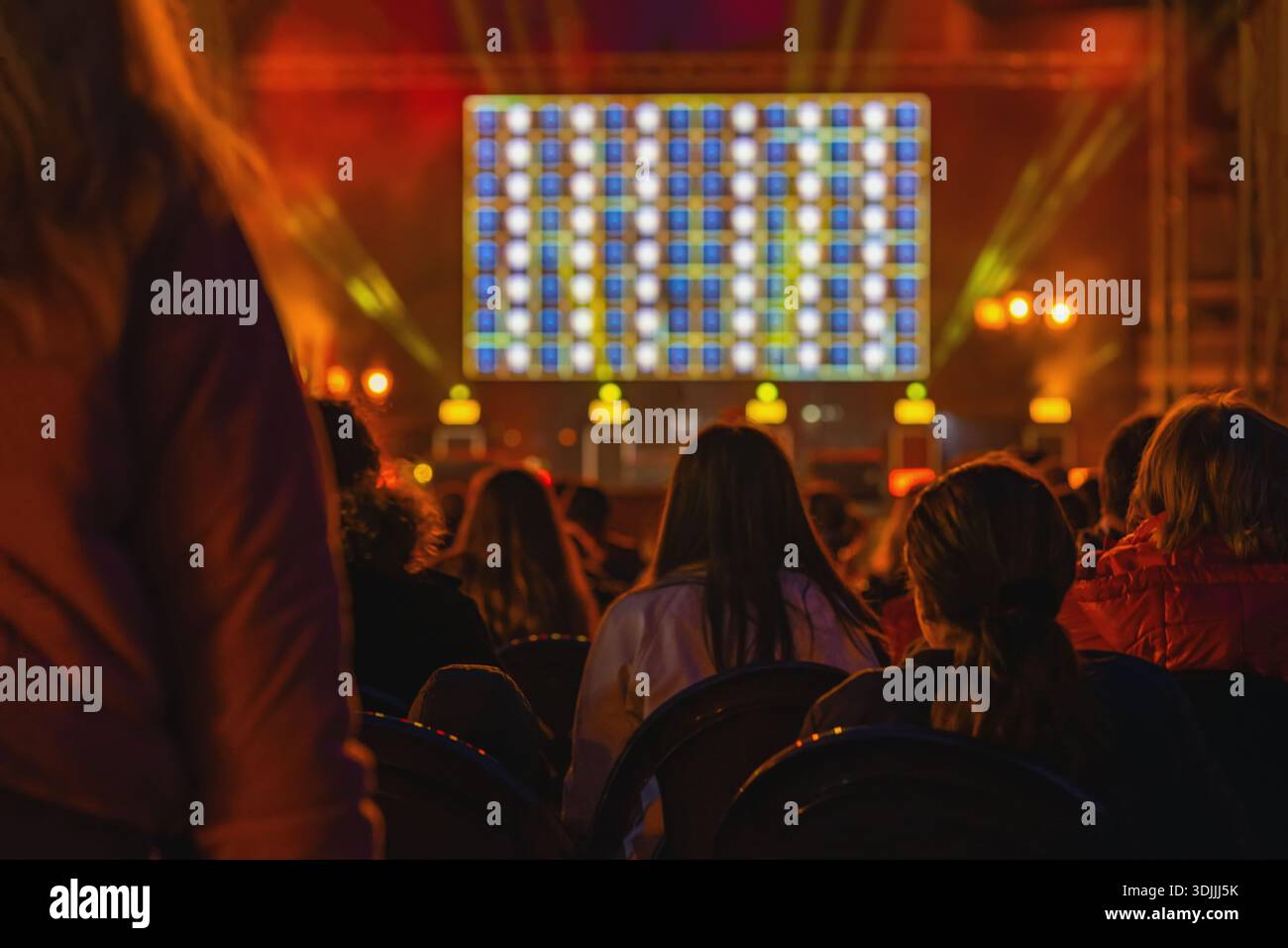 Audience watching illuminated stage with giant digital screen during ...