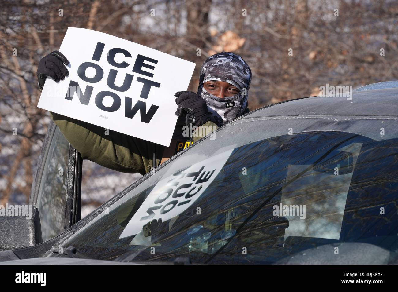 A federal officer holds up a "ICE Out Now" sign during a traffic stop ...