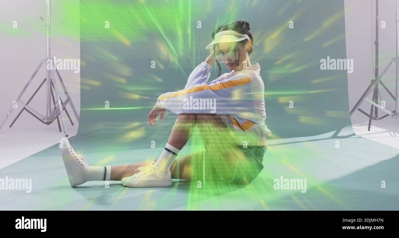 Posing female model touching visor while sitting on teal backdrop ...