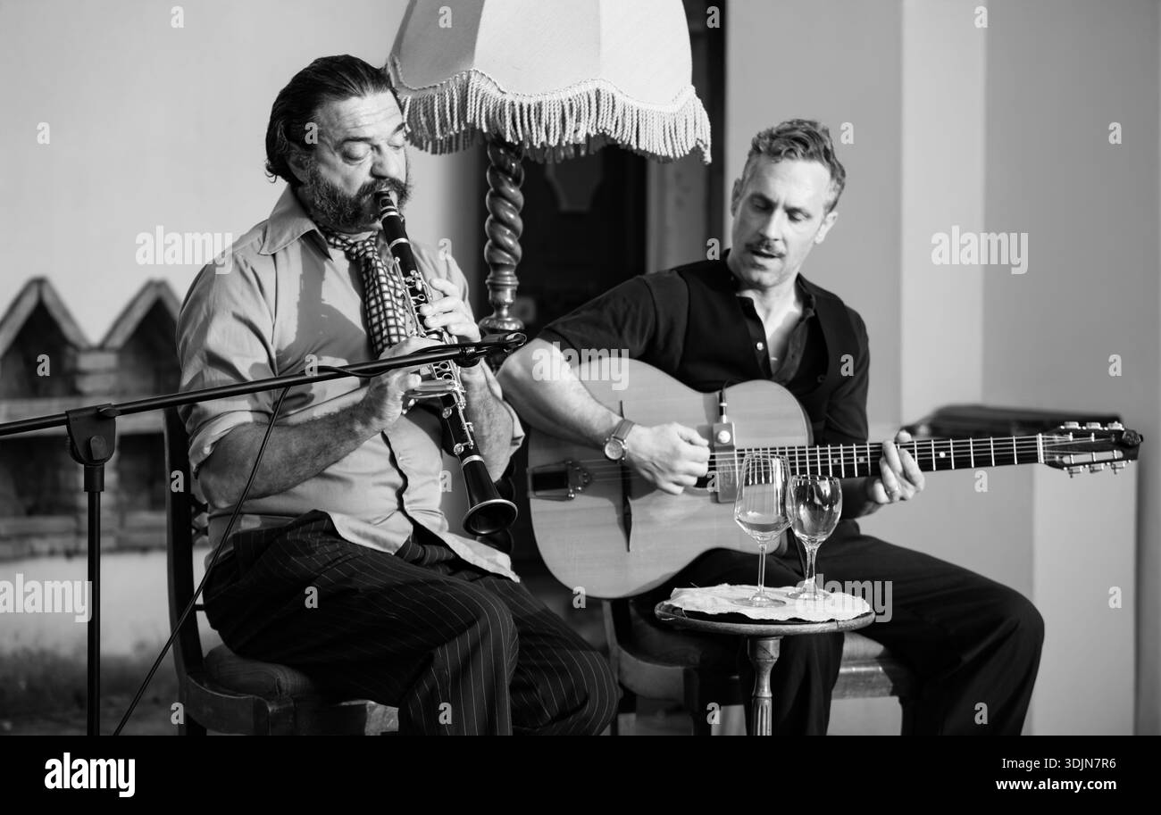 Side profile of a male artist in a patterned tie blowing a brass horn ...