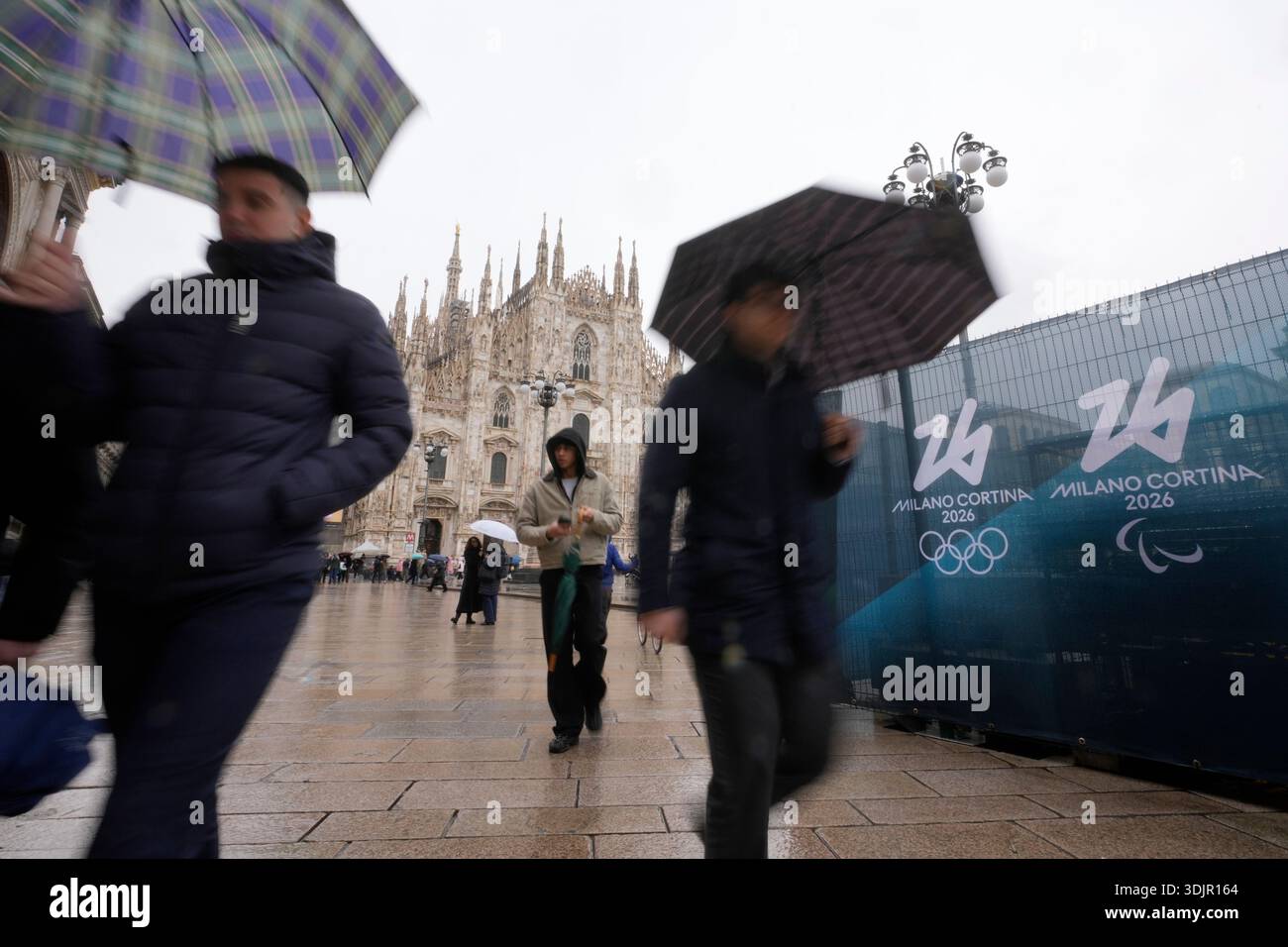 People walk under the rain in front of the Duomo gothic cathedral, in ...