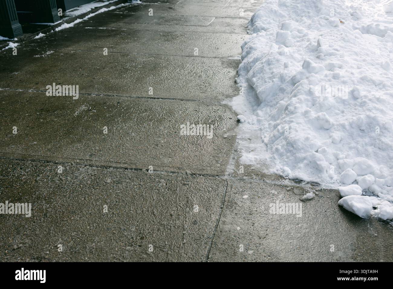 Snow builds up on the side of the sidewalk near a city building during ...