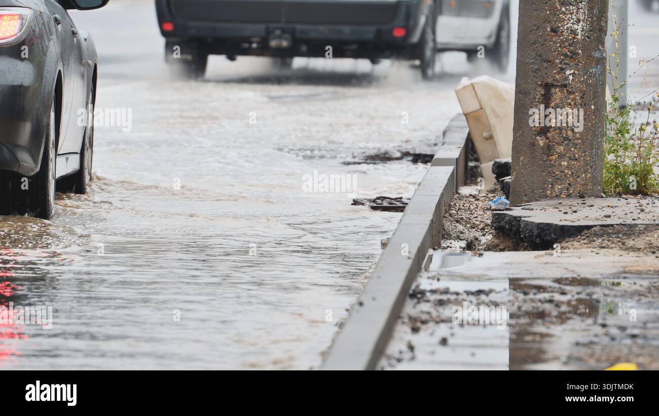 Cars driving through deep puddles on a flooded street during heavy rain ...