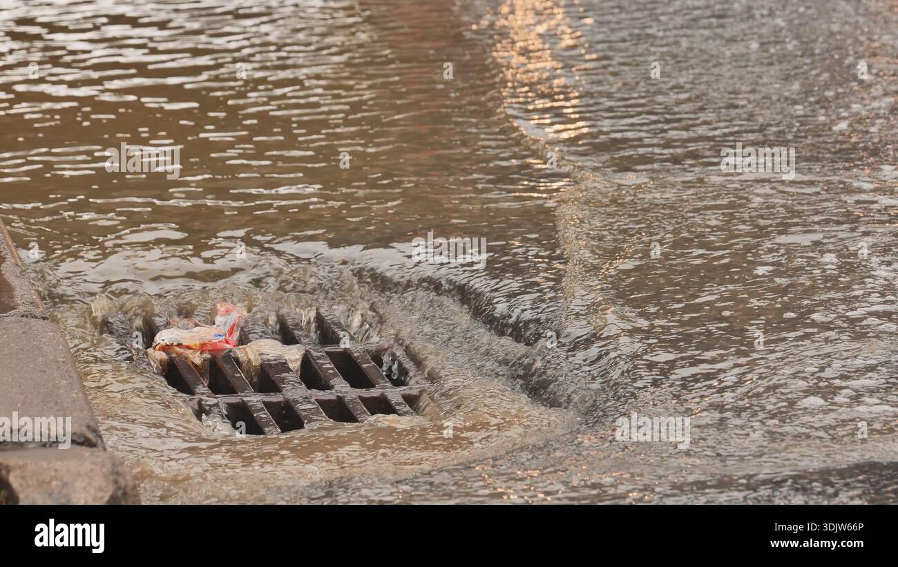 Car wheel splashing through muddy floodwater on a street, a storm drain ...